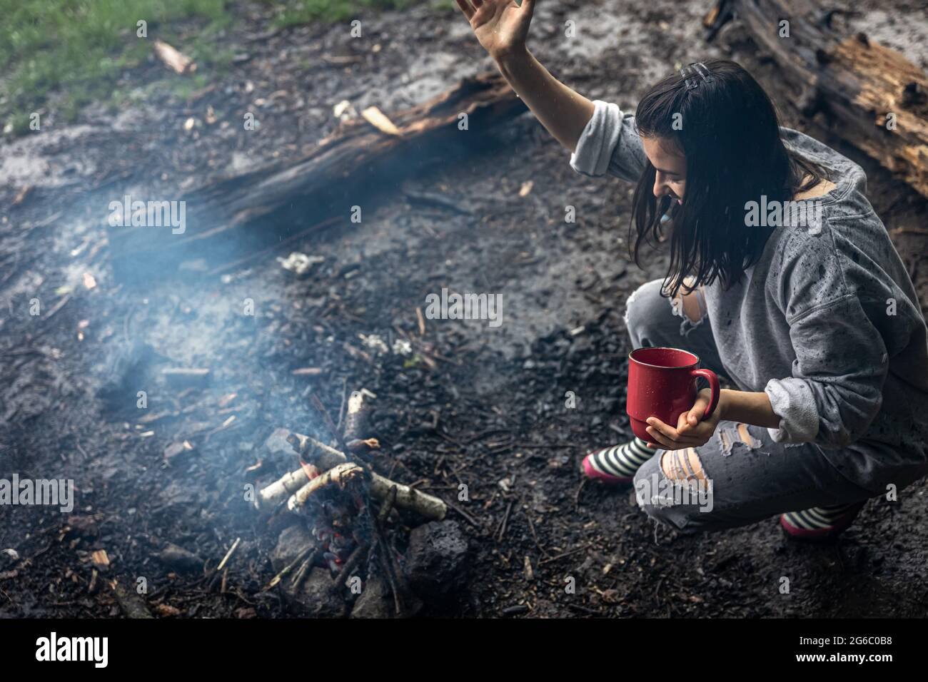 A girl with a cup in her hand is fanning the fire to keep warm Stock ...