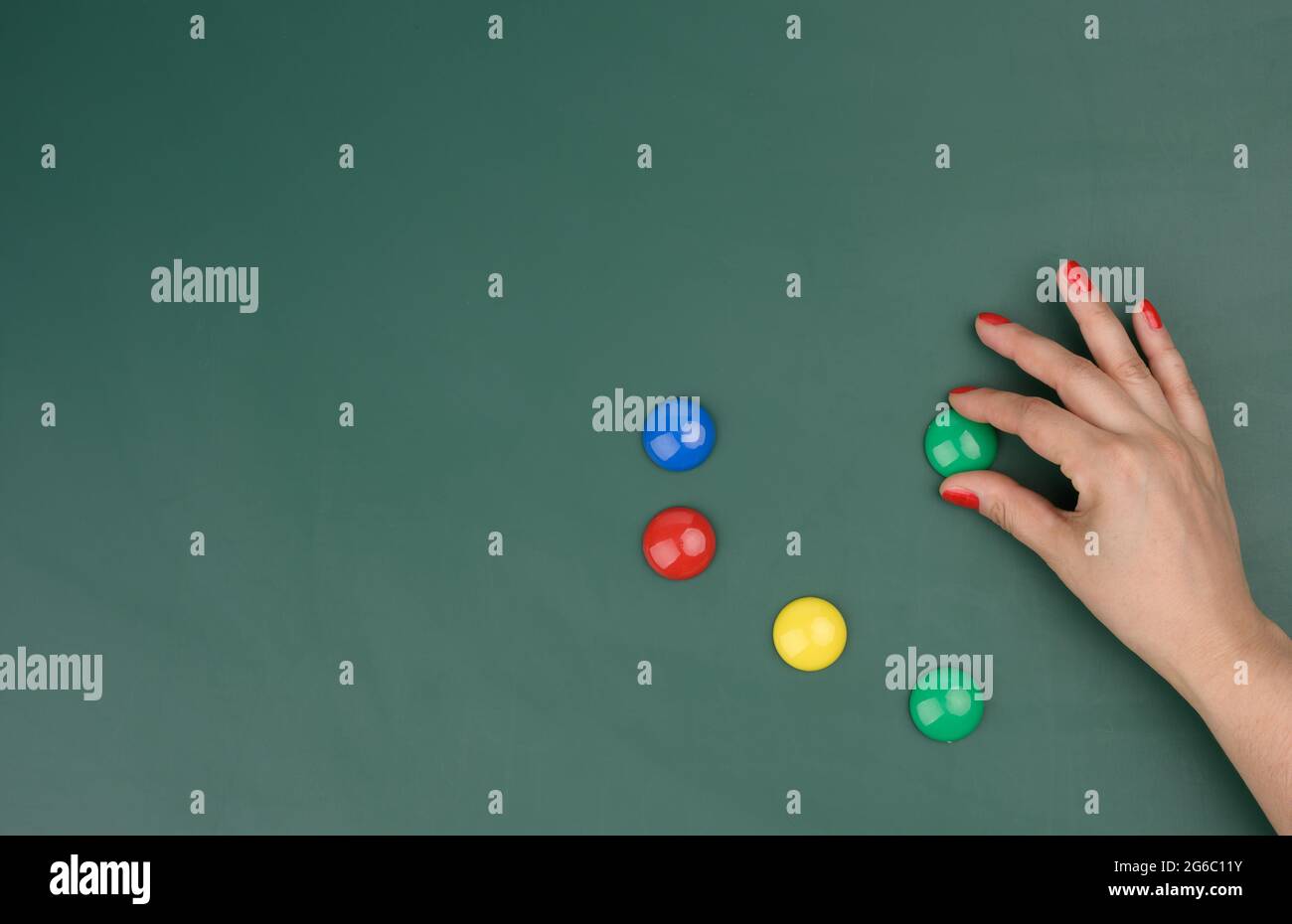 female hand attaches multi-colored magnets to a green board, place for ...
