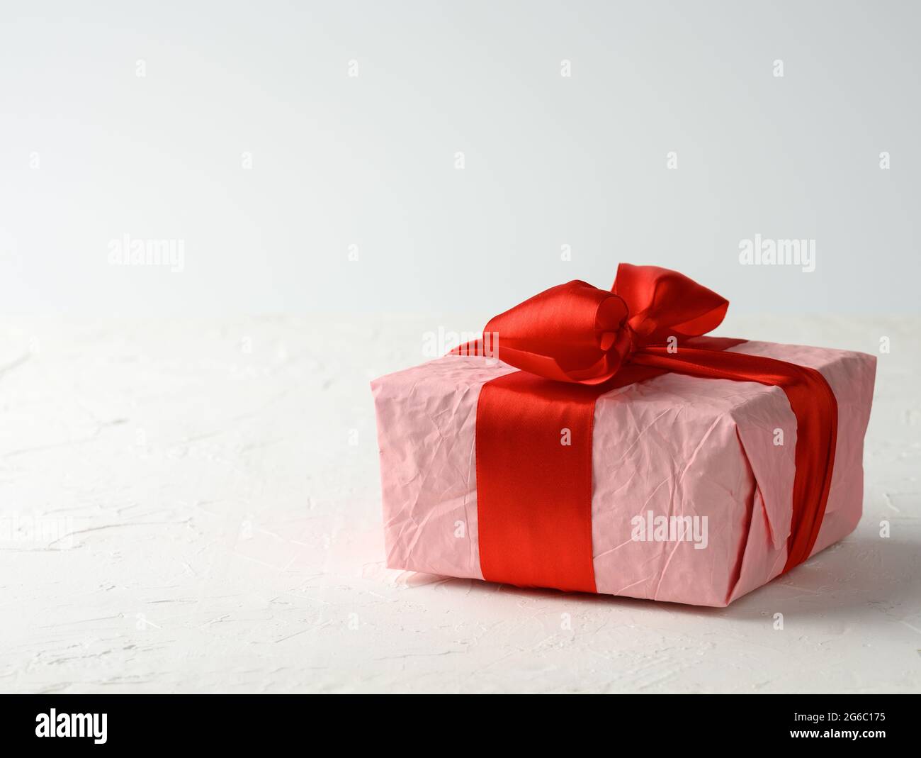 square box wrapped in pink paper tied with red silk ribbon on white ...