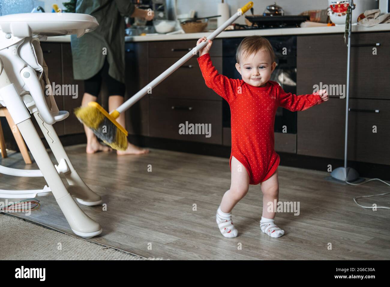 Little mothers helper. Cute toddler baby girl with mop help her mom do ...