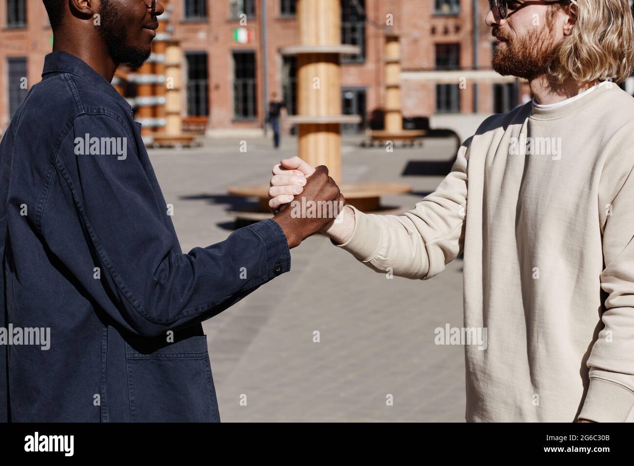 Side view portrait of two men greeting each other outdoors in city with ...