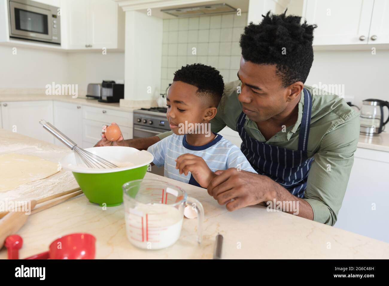 African american father and son baking in kitchen breaking eggs into ...