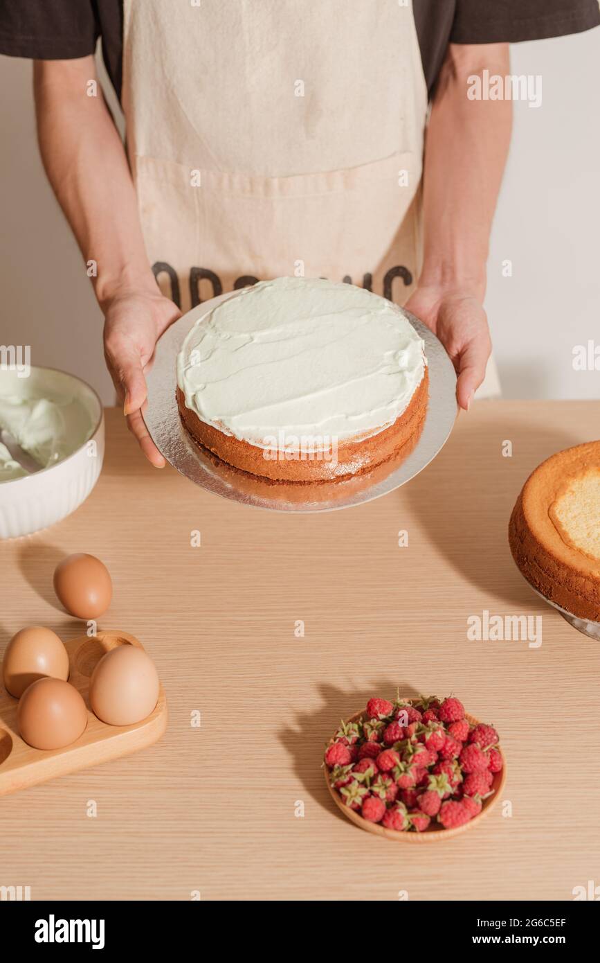 Male pastry chef is holding sponge cake with many various ingredients ...