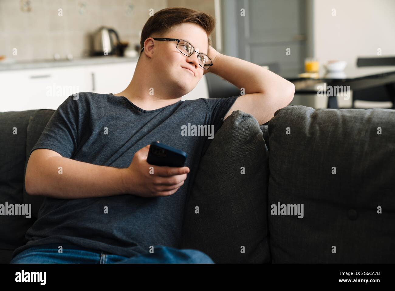 Young man with down syndrome using cellphone while sitting on couch at ...
