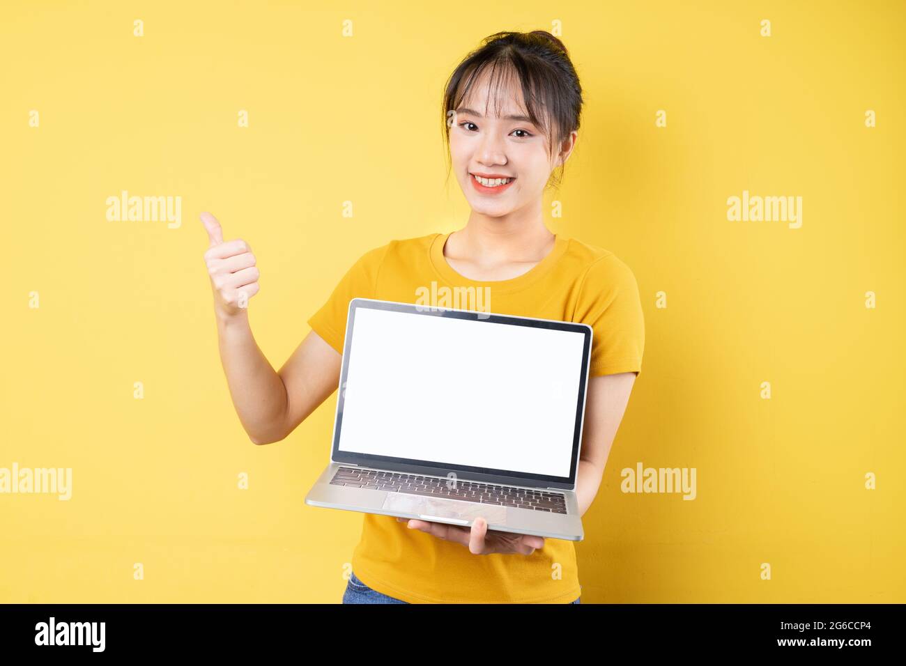 portrait of young girl holding laptop in hand on yellow background ...