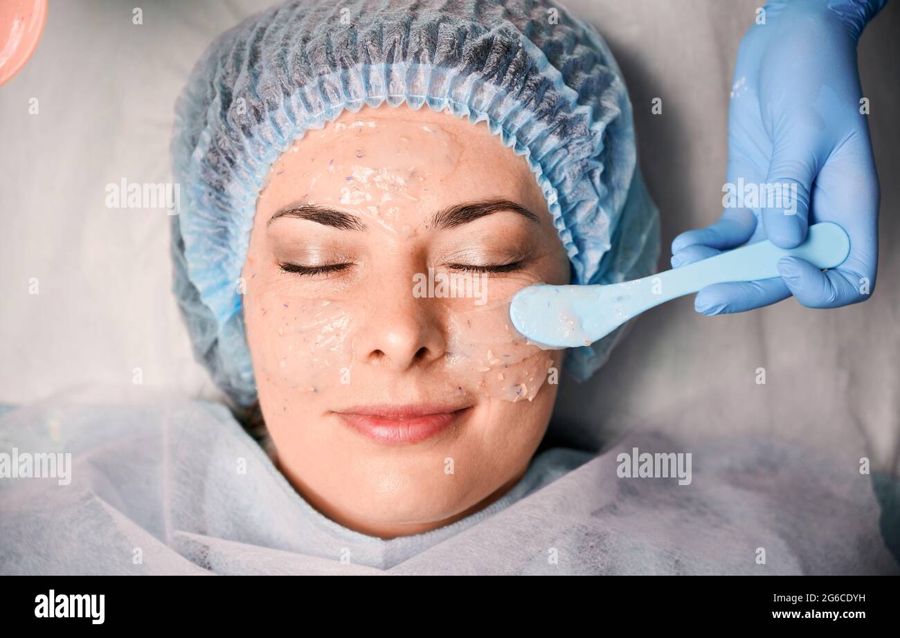 Close up of beautician hand applying cosmetic mask on young woman face ...