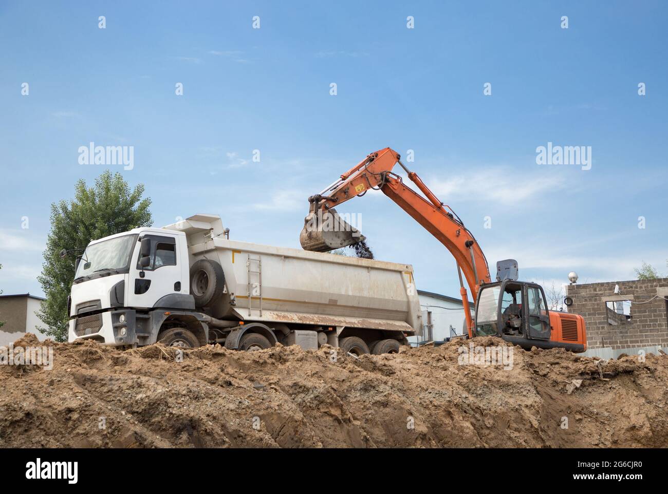 orange crawler excavator and gray dump truck during excavation phase at construction site ...