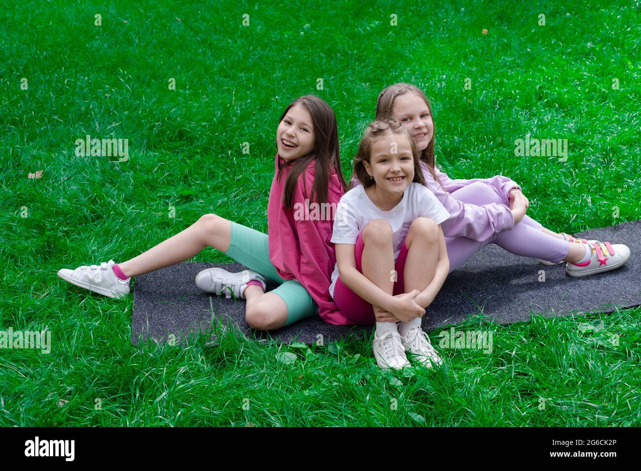 three beautiful happy tween teenagers girls in colorful clothes sitting ...