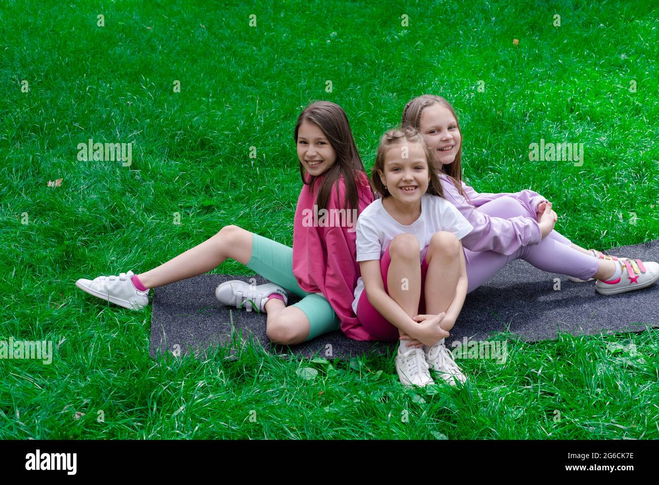 three beautiful happy tween teenagers girls in colorful clothes sitting ...