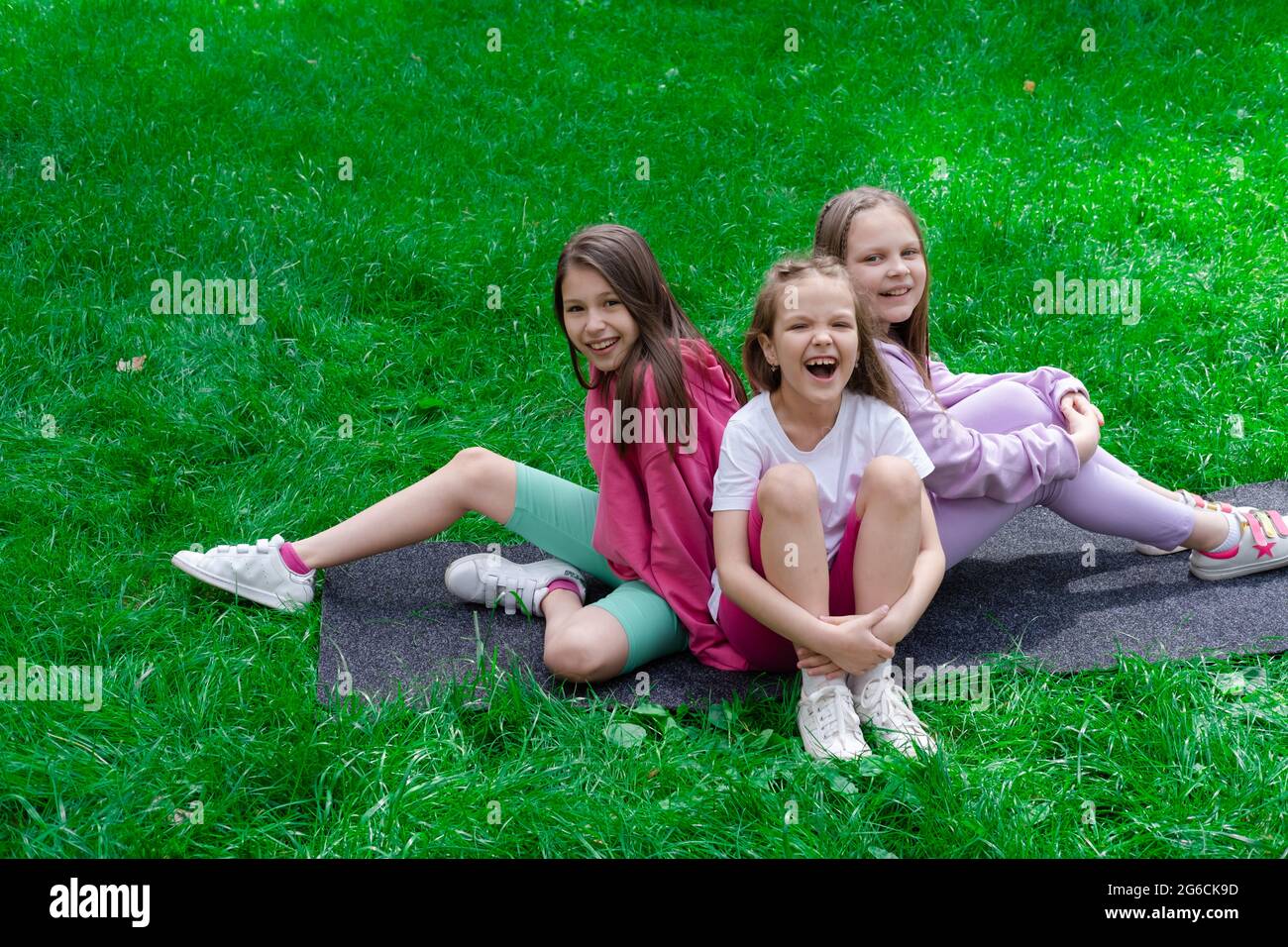three beautiful happy tween teenagers girls in colorful clothes sitting ...