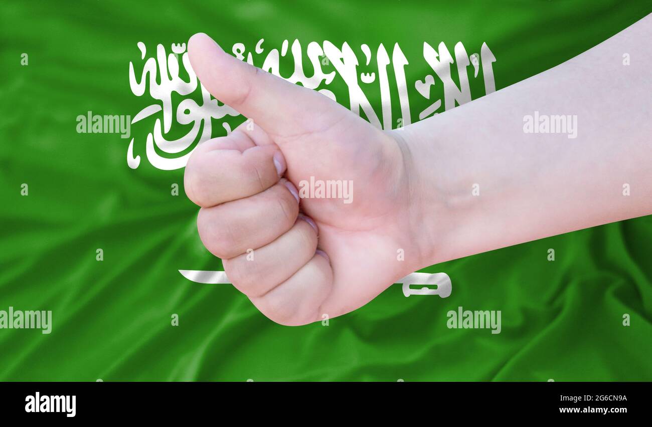 Hand makes a thumbs up sign on the background of the flag of Saudi ...