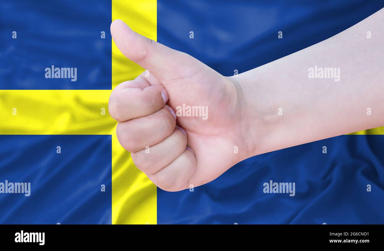 Hand makes a thumbs up sign on the background of the flag of Sweden ...