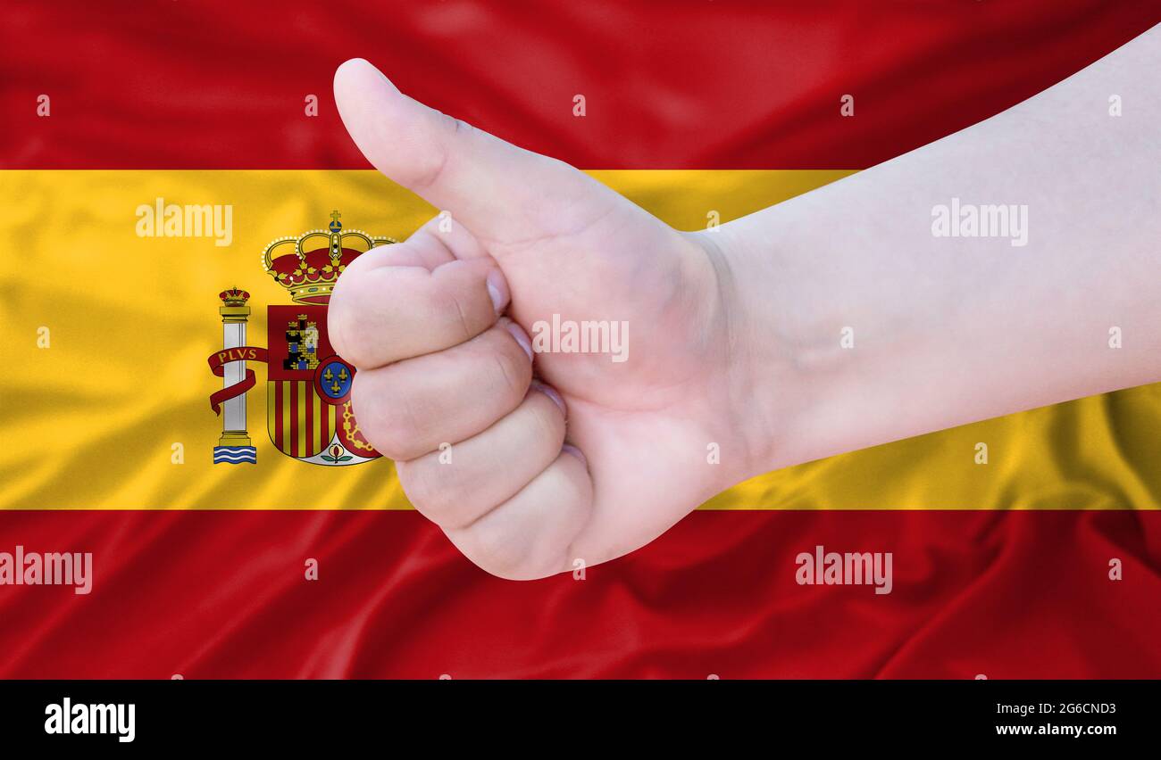 Hand makes a thumbs up sign on the background of the flag of Spain ...