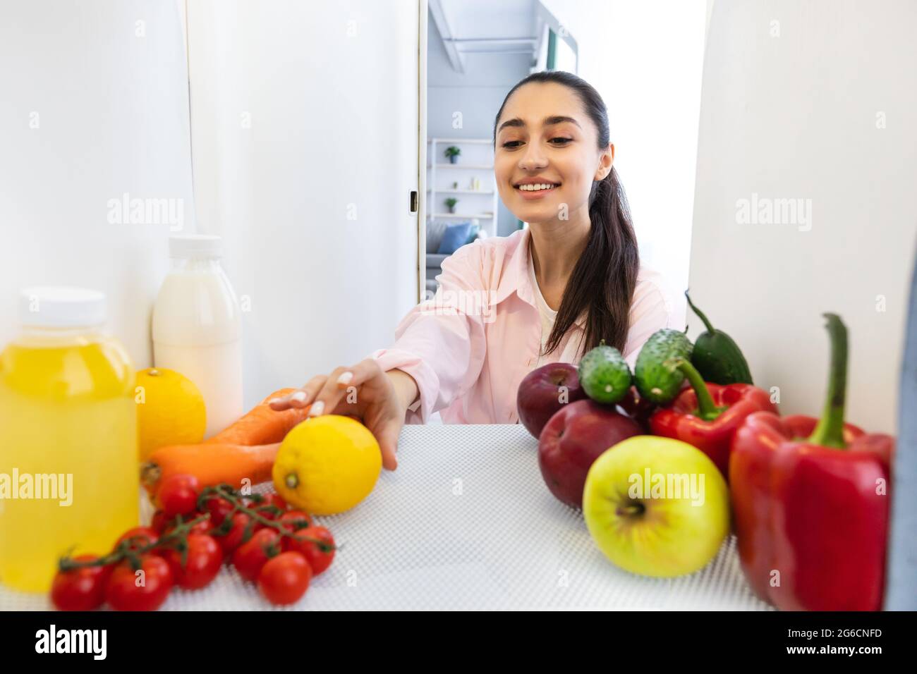Smiling woman opening fridge and taking fresh food Stock Photo - Alamy