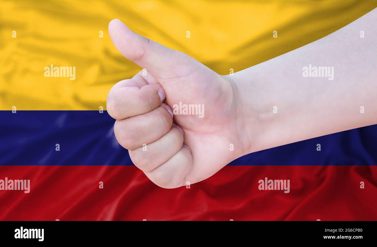 Hand makes a thumbs up sign on the background of the flag of Colombia ...