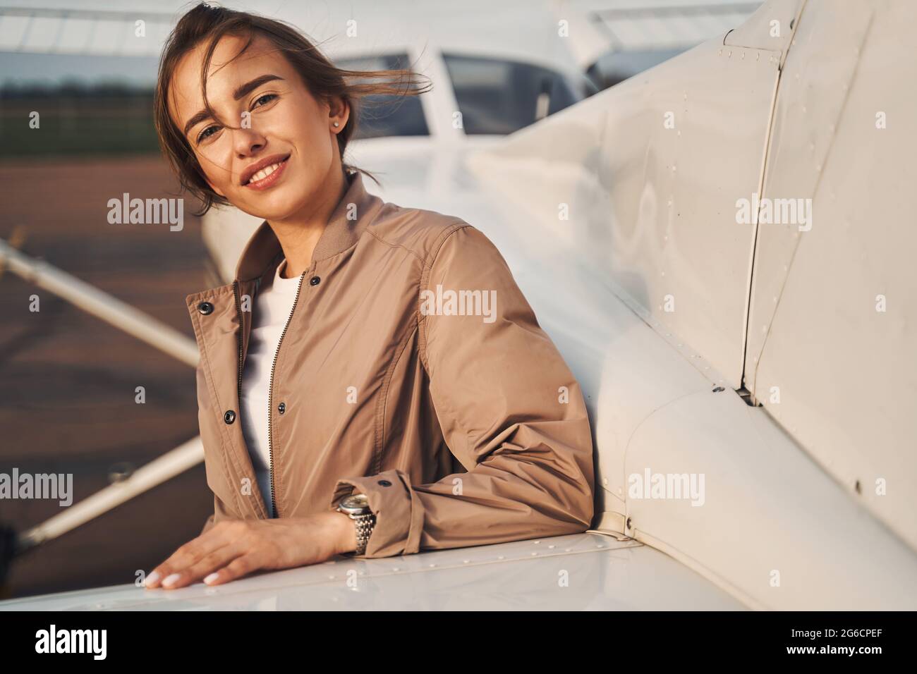 Cheerful young woman standing near plane at airdrome Stock Photo - Alamy
