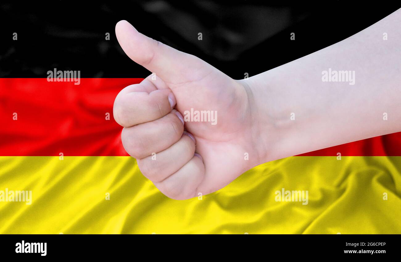 Hand makes a thumbs up sign on the background of the flag of Germany ...