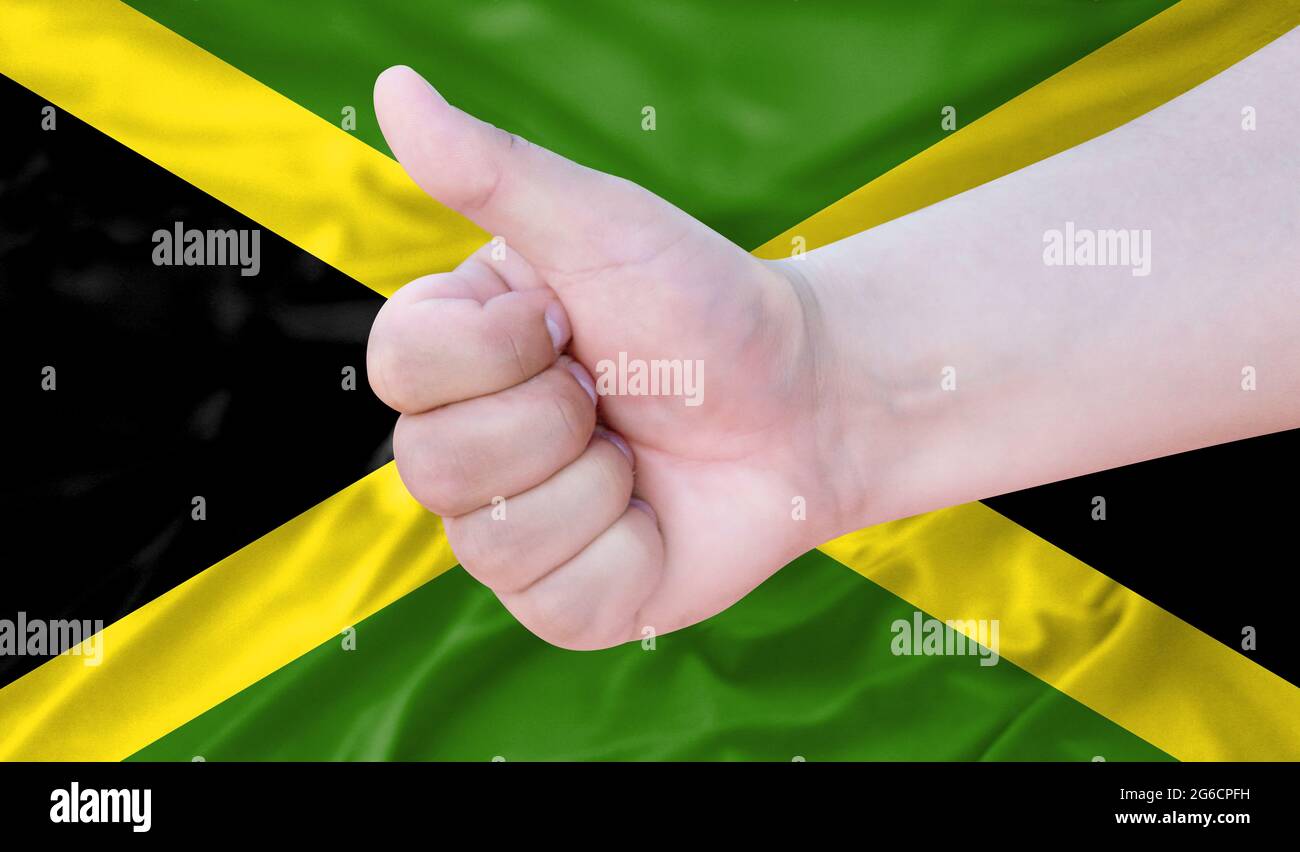 Hand makes a thumbs up sign on the background of the flag of Jamaica ...