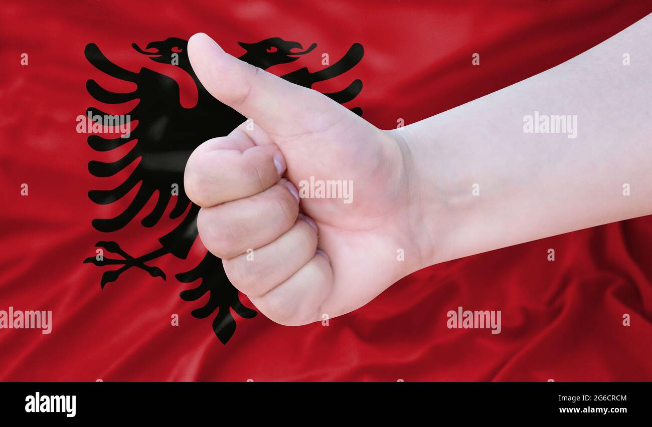 Hand makes a thumbs up sign on the background of the flag of Albania ...