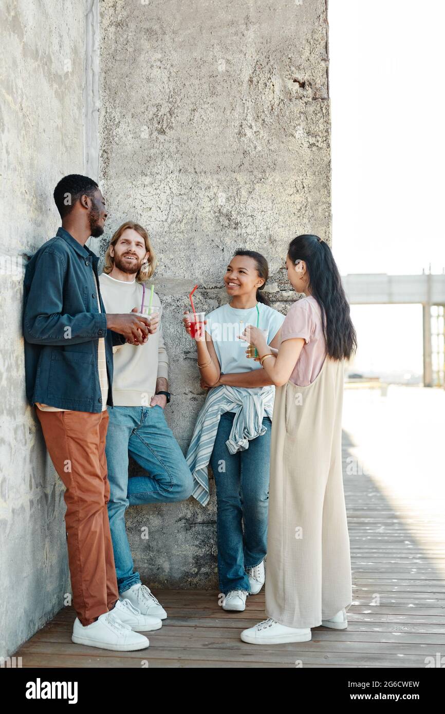 Vertical full length portrait of diverse group of young people chatting ...