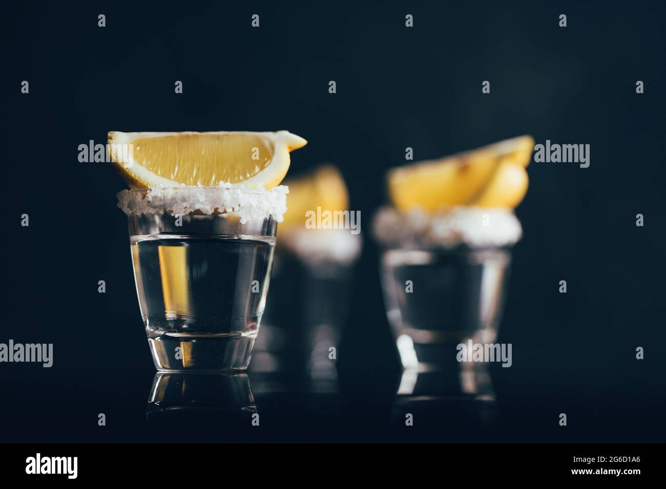 Tequila shots with salt and lemon placed on reflective surface against ...