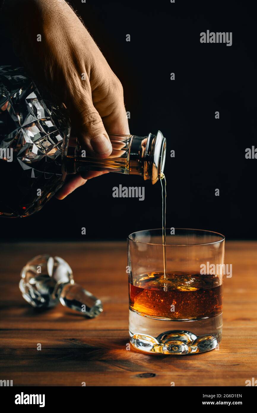 Glass of cold whiskey with ice placed on wooden table near decanter on ...
