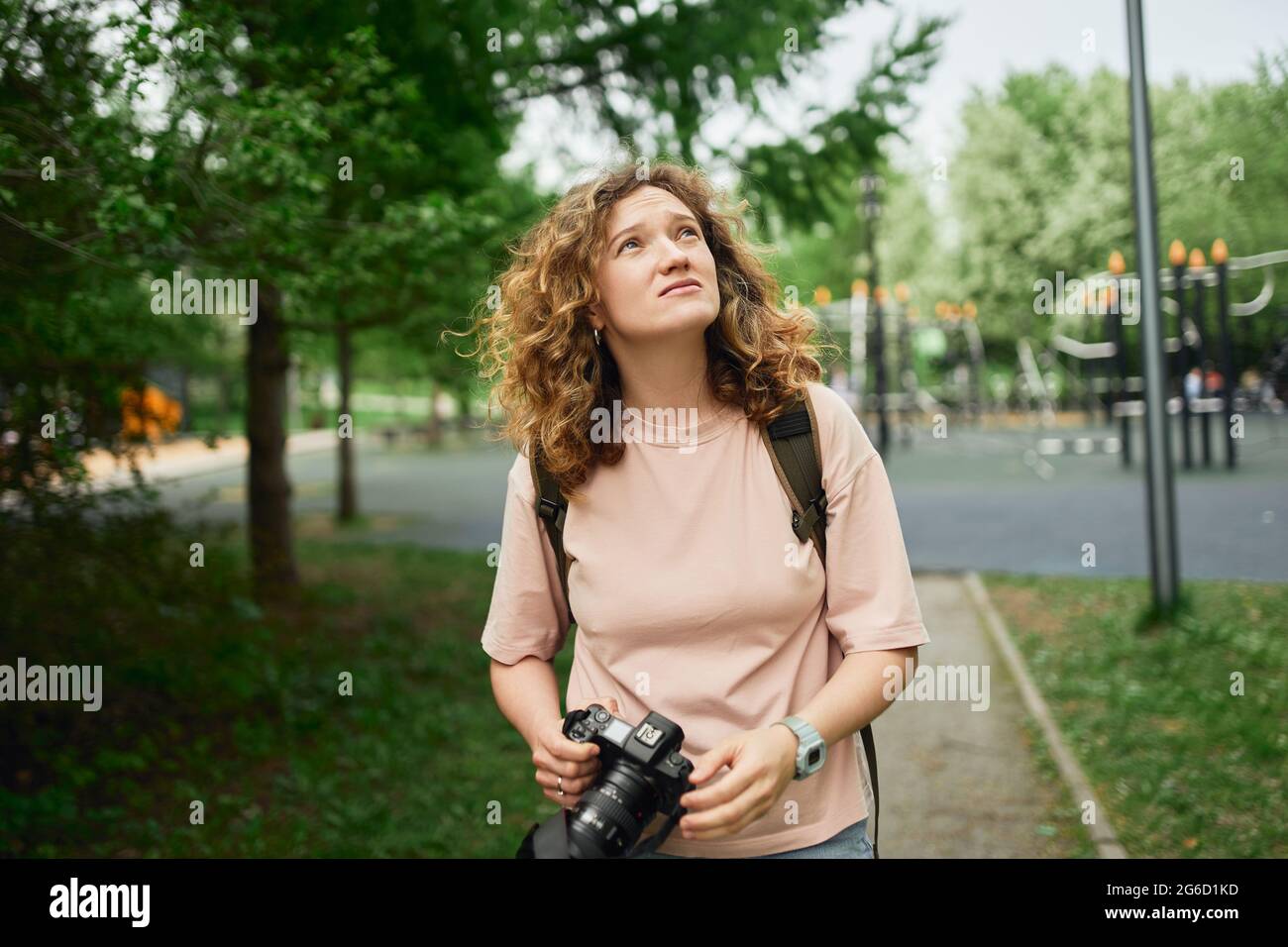 Focused female photographer with modern camera standing in green park ...