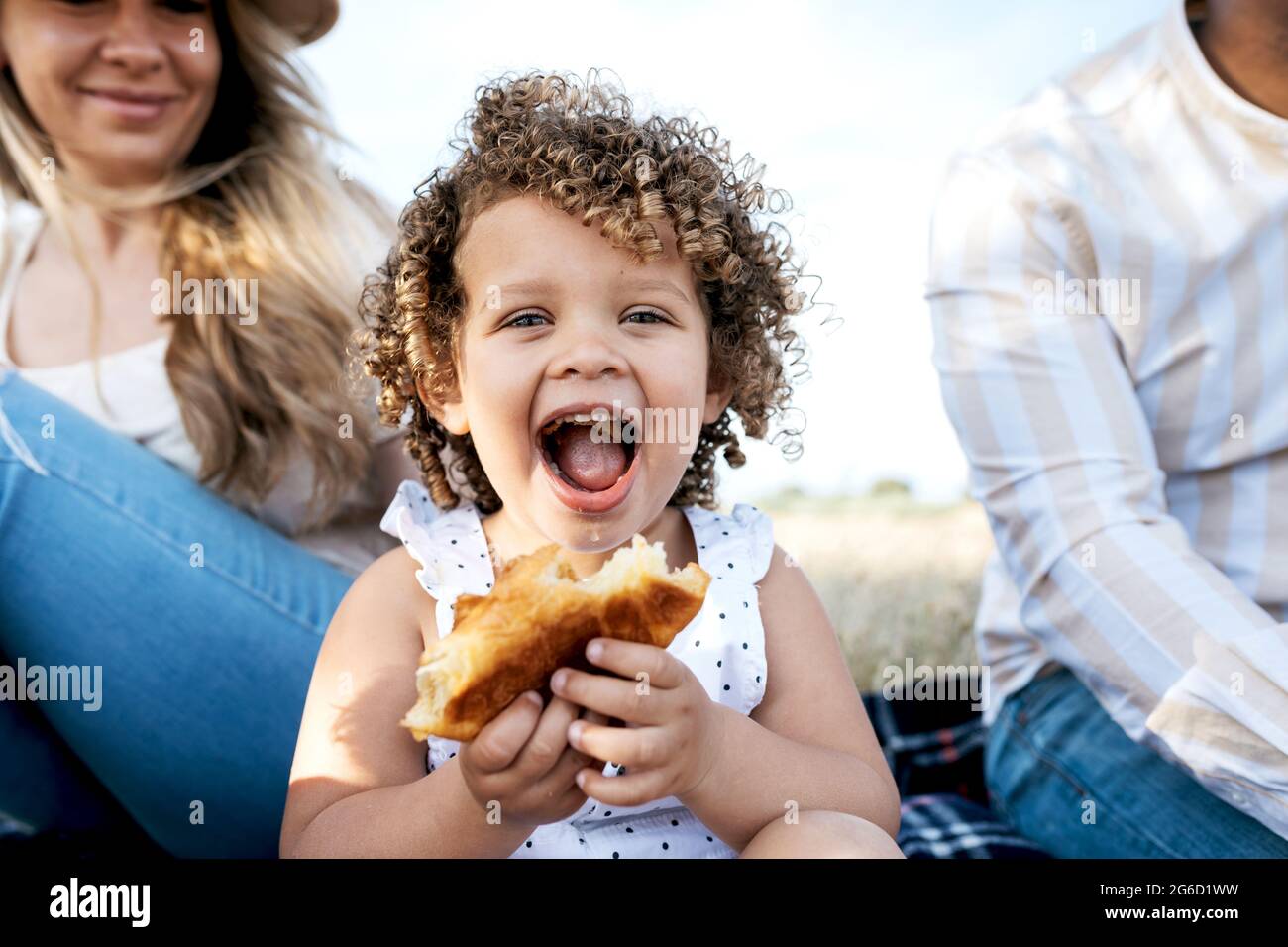 Cheerful little girl eating pastry looking at camera sitting with ...