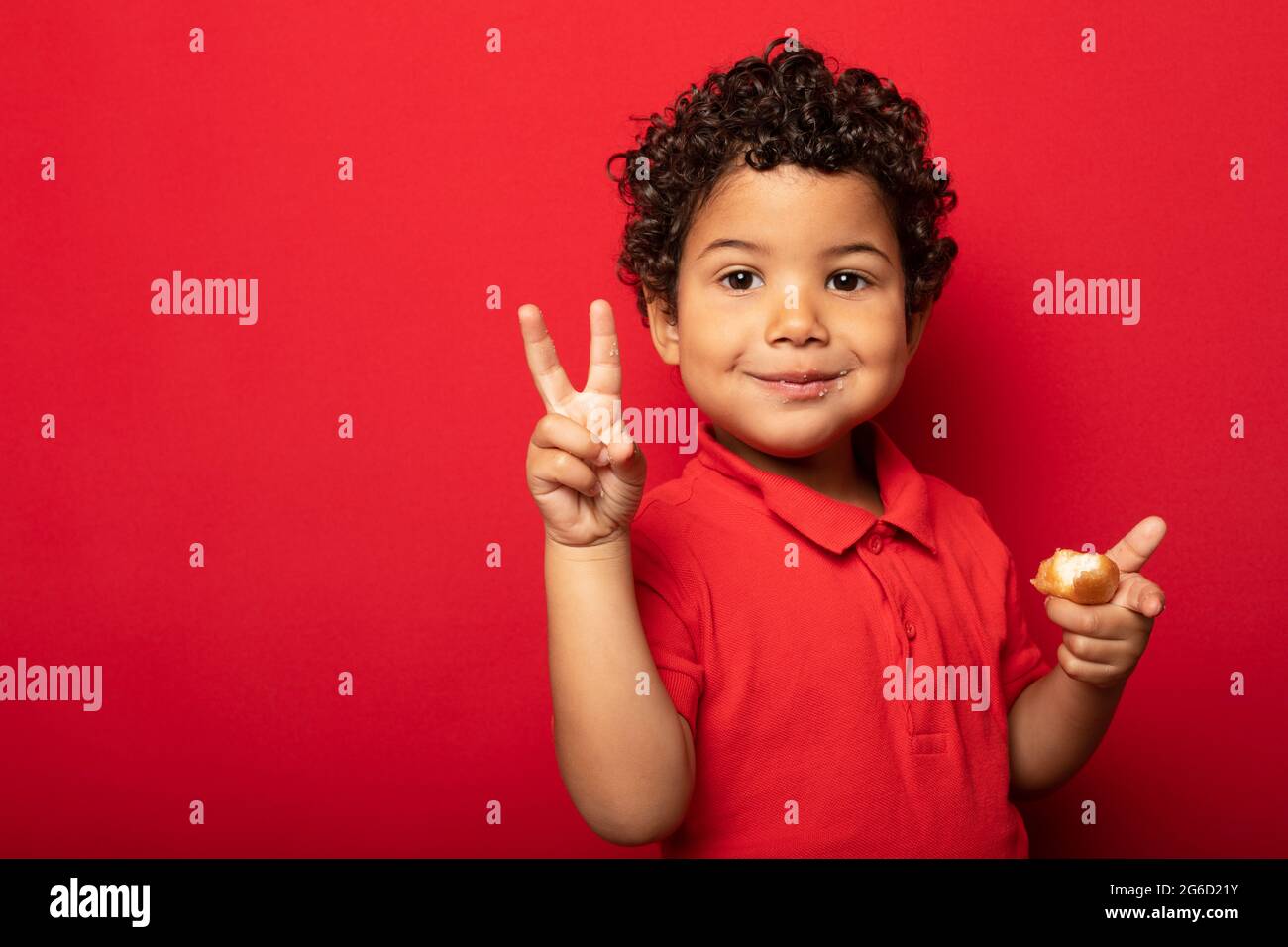 Adorable child eating delicious doughnut and showing V sign while ...