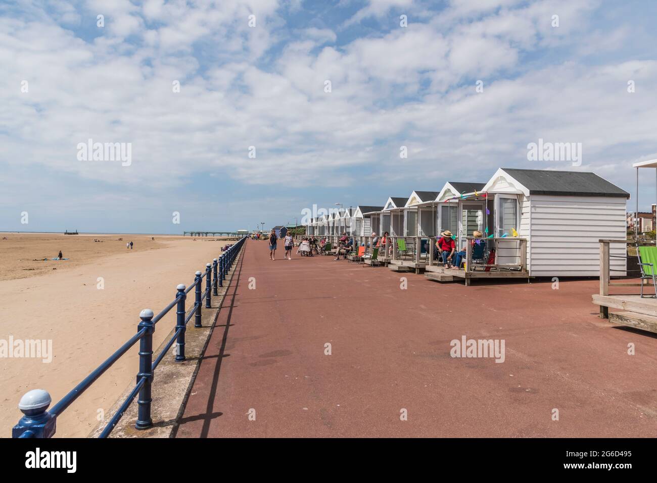 The image is of the seafront promenade and colourful beach-huts at the ...