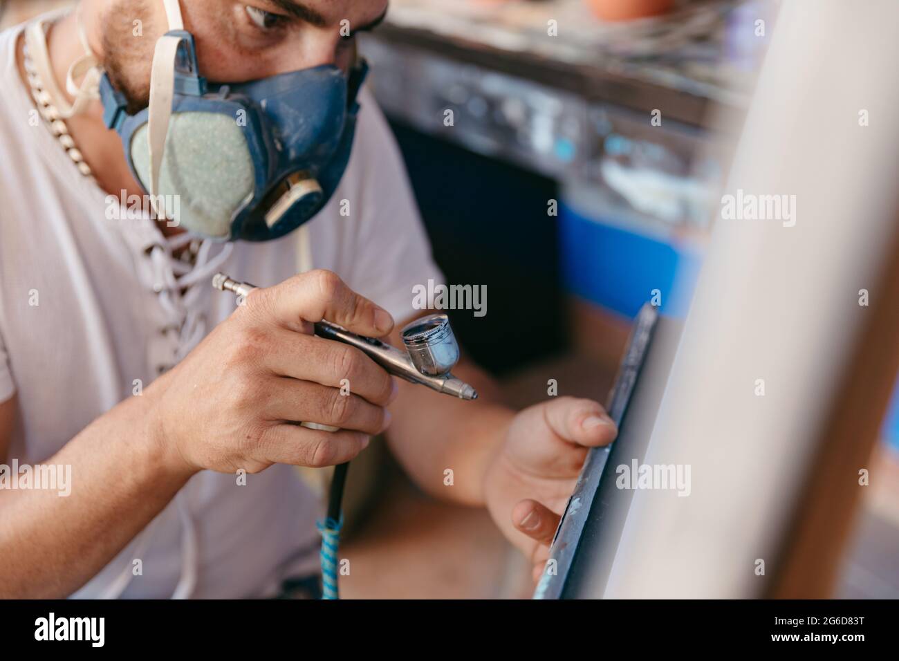 Side view of cropped male artist in respirator using spray gun to paint ...