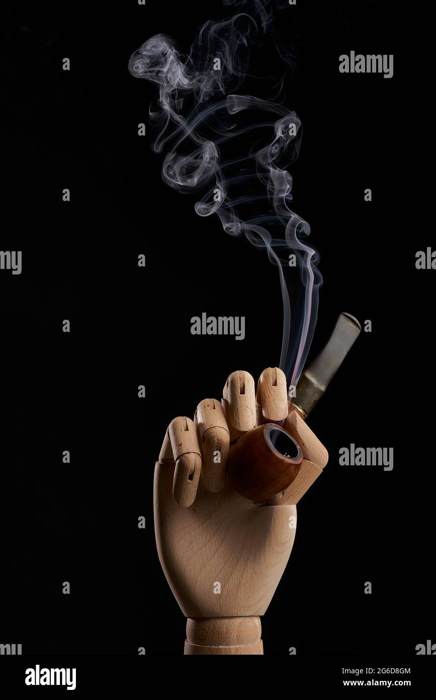 Traditional tobacco pipe with smoke in wooden hand on black background ...