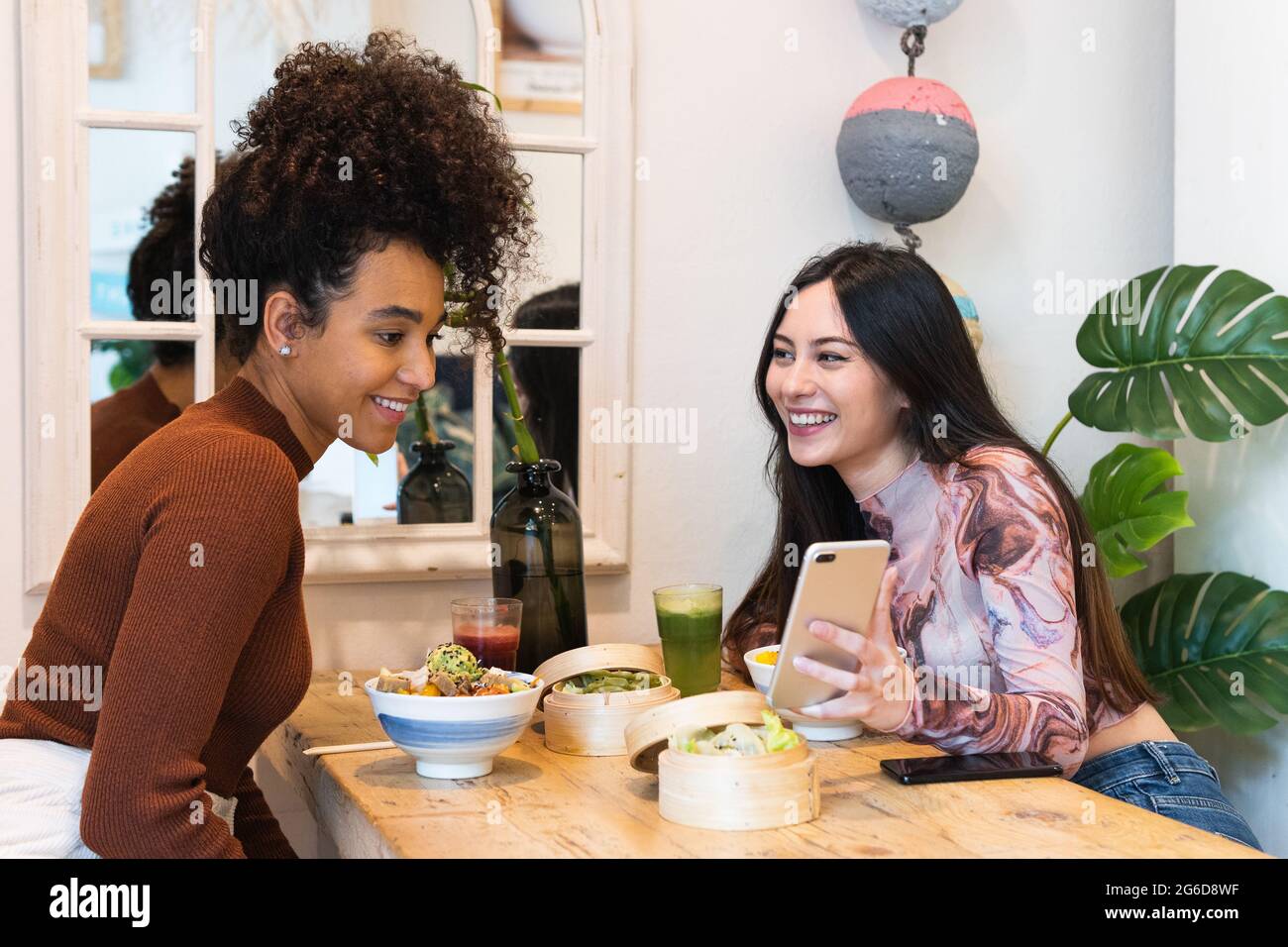 Cheerful diverse female friends sitting at table with poke in ...