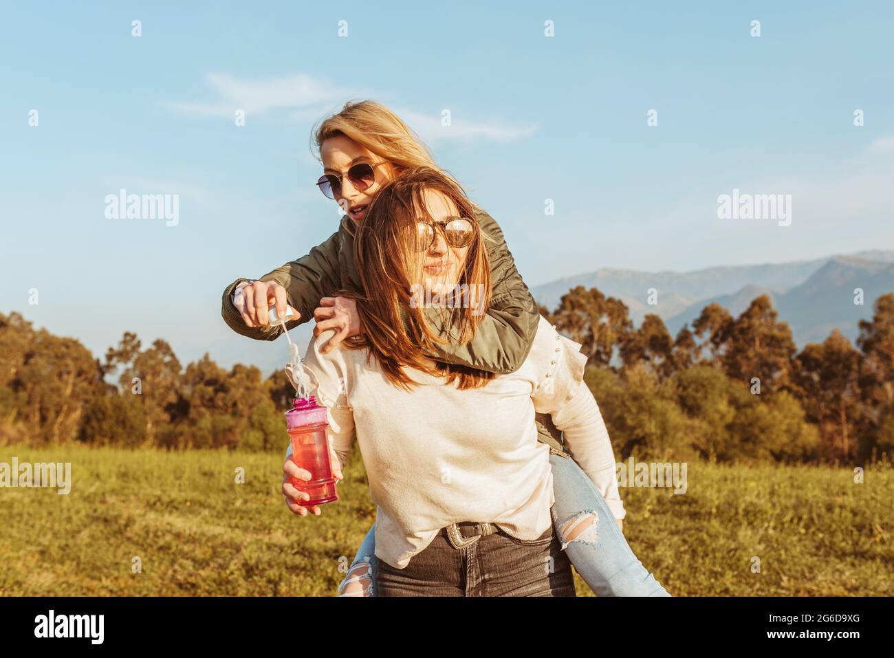Laughing blond Woman giving piggyback ride to cheerful girlfriends ...