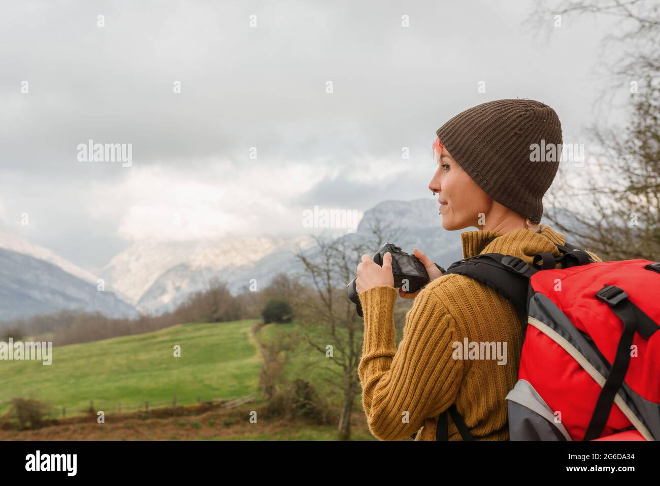 Side view of female backpacker taking picture of mountainous landscape ...