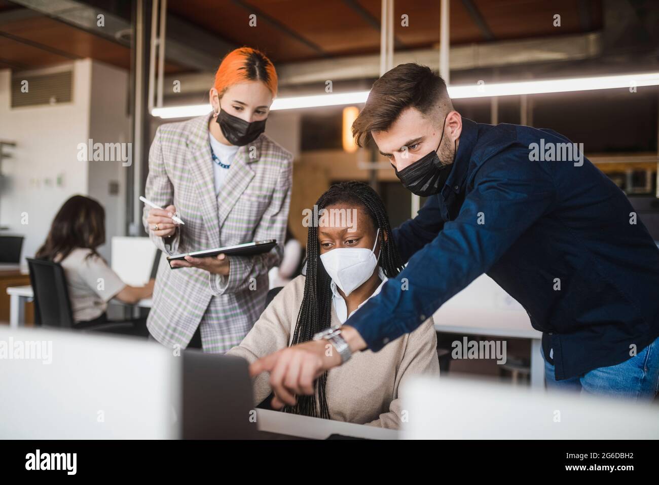 Group of diverse coworkers in protective masks gathering at table with ...