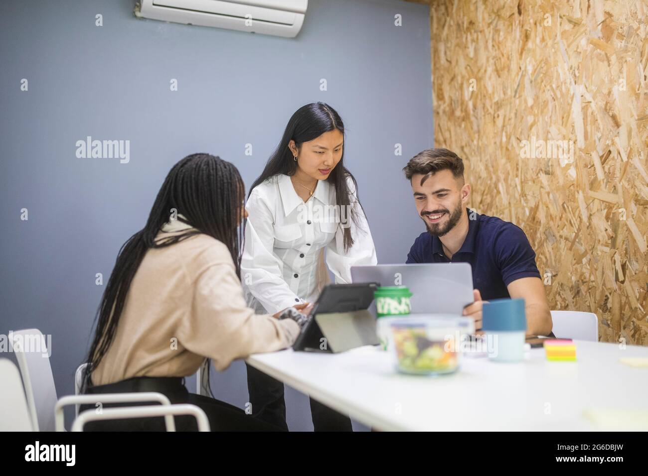 Group of multiracial content coworkers gathering at table and using ...