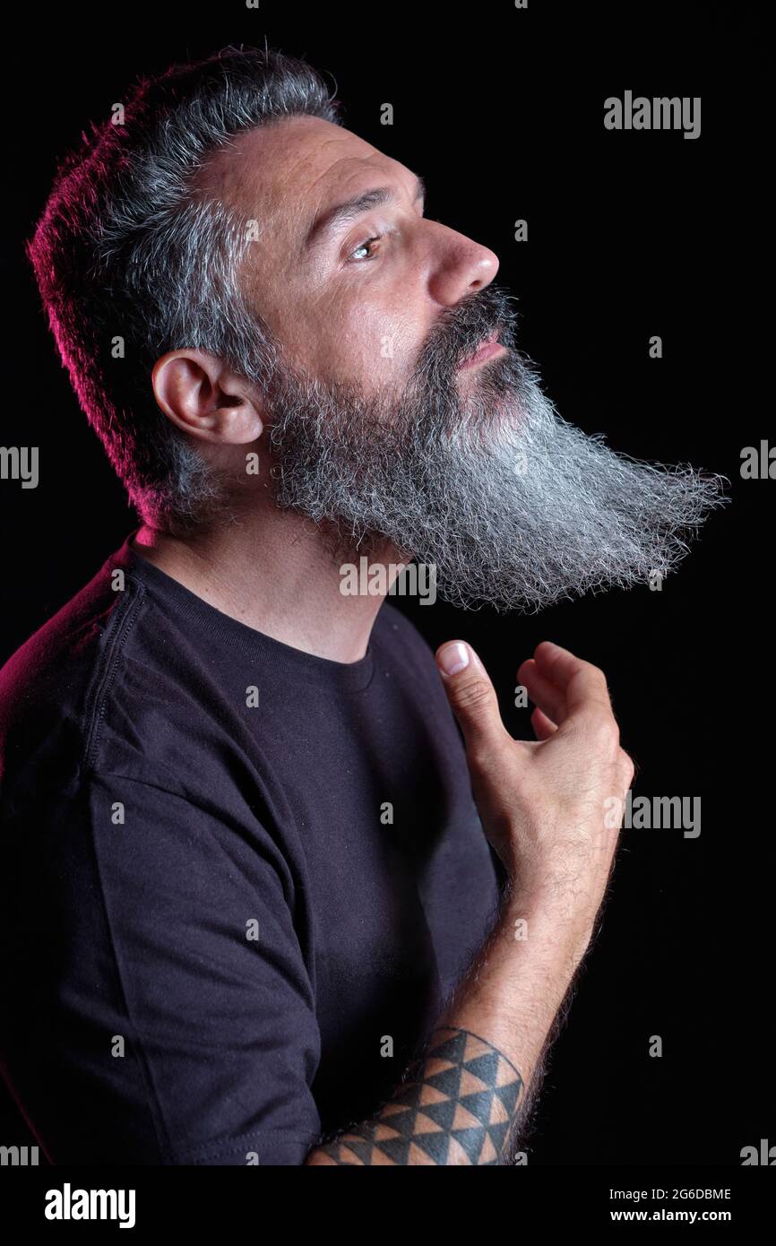 Side view of handsome mature male with gray beard on black background ...