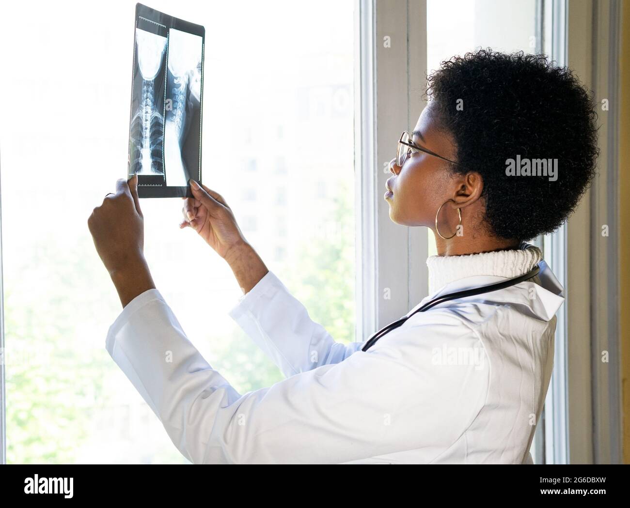 Side view of young black female medic standing near window and ...