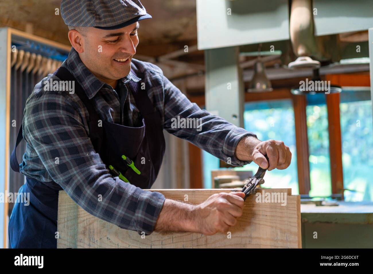 Cheerful male joiner smoothing timber plank with professional ...