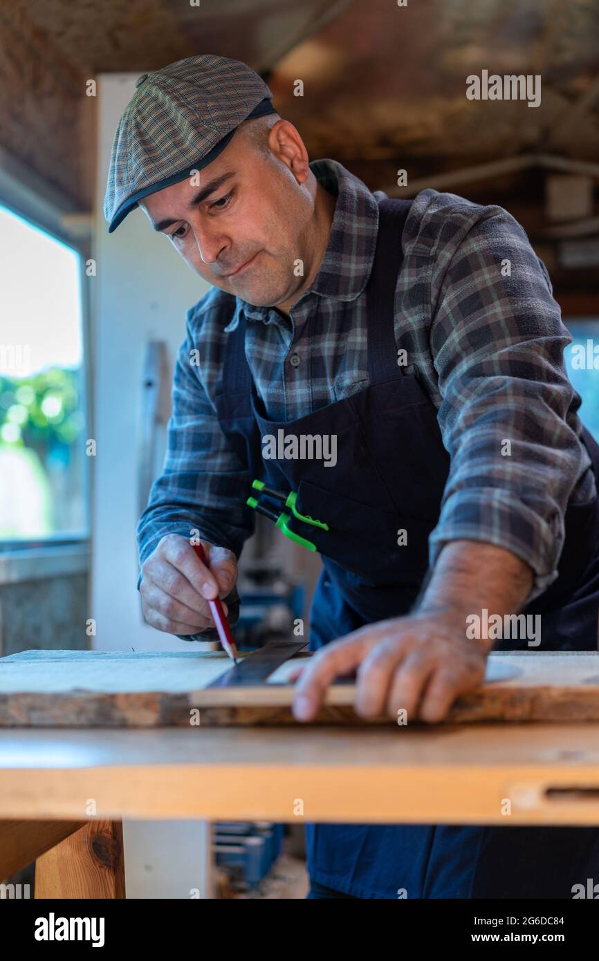 Skilled adult male woodworker with pencil and ruler marking wooden ...