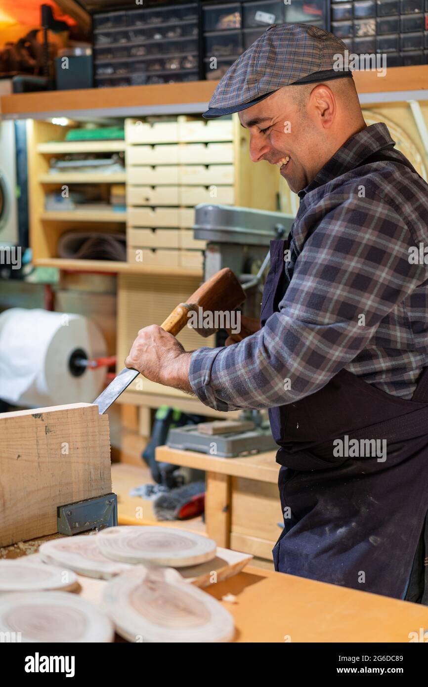 Side view of cheerful mature male master using hammer and chisel while ...