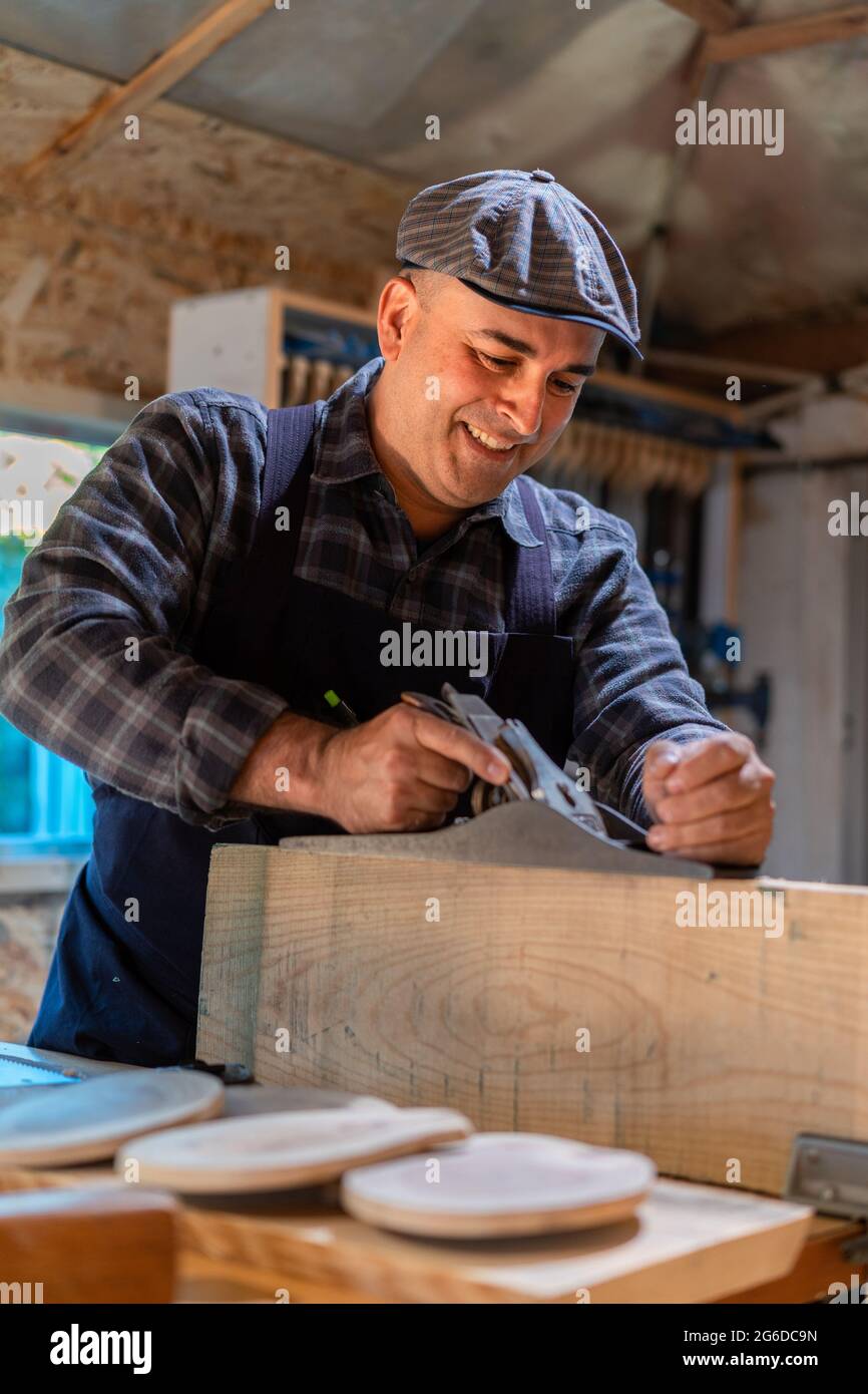 Cheerful male woodworker smoothing wooden detail with jack plane while ...