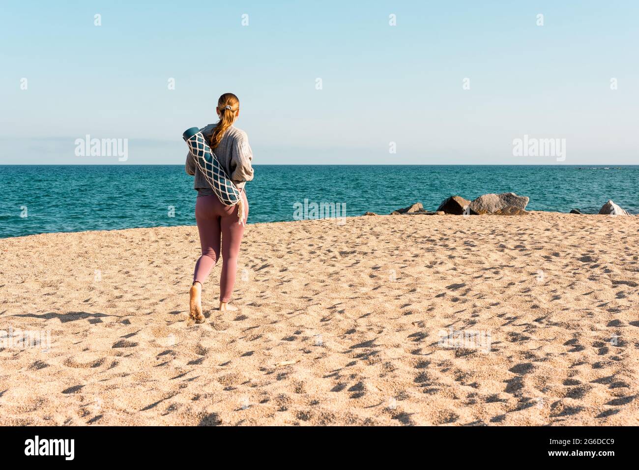 Full body back view of unrecognizable of young barefoot female in activewear with rolled yoga ...