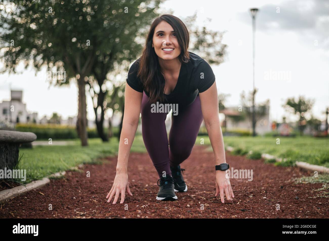 Cheerful ethnic female runner standing in crouch start position ready ...