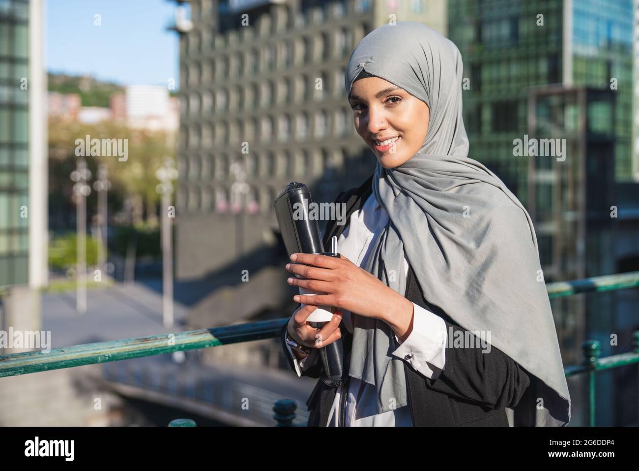 Cheerful Muslim female entrepreneur in hijab and with takeaway coffee ...