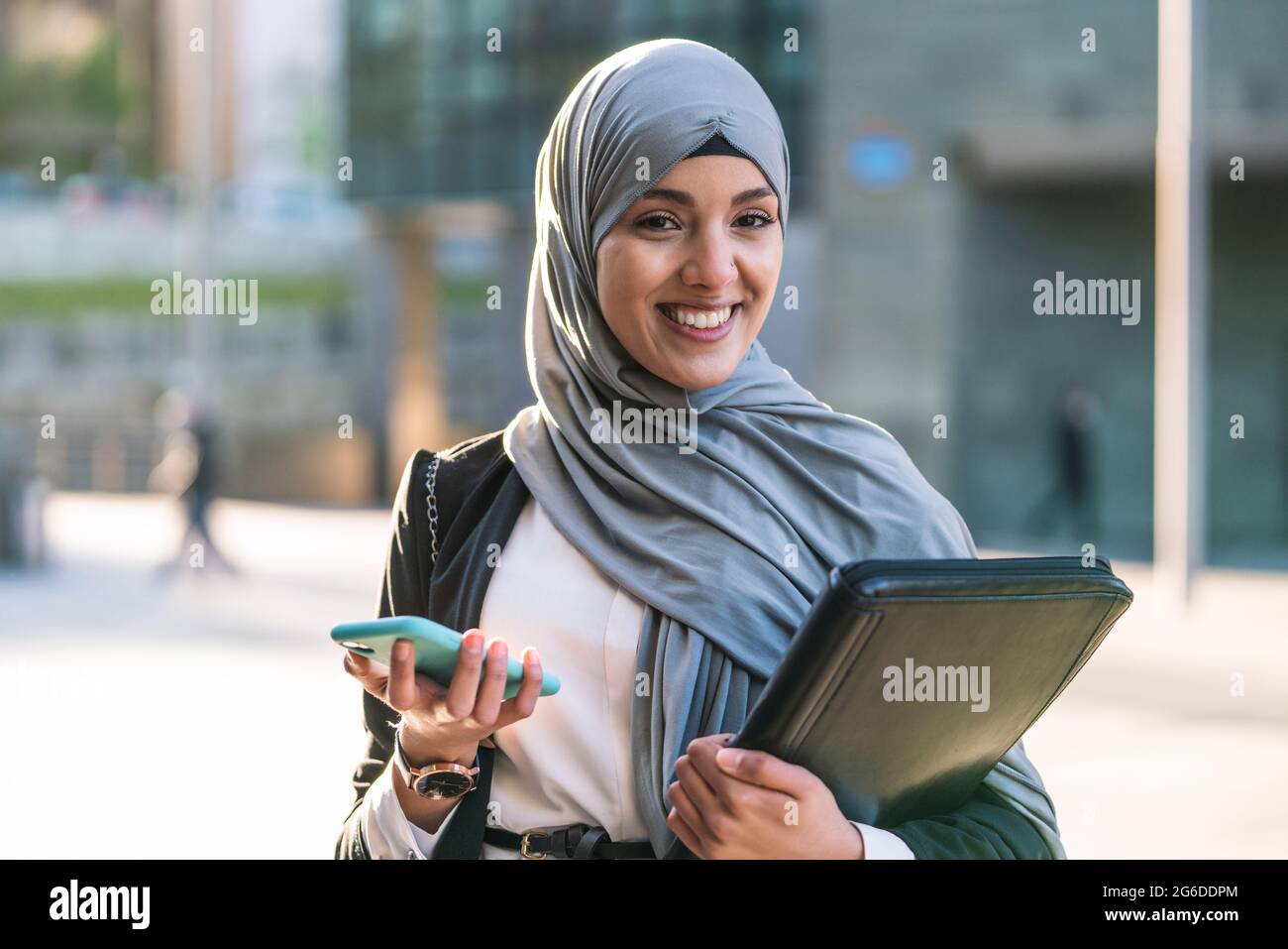Happy Muslim female entrepreneur in hijab and with folder standing in ...