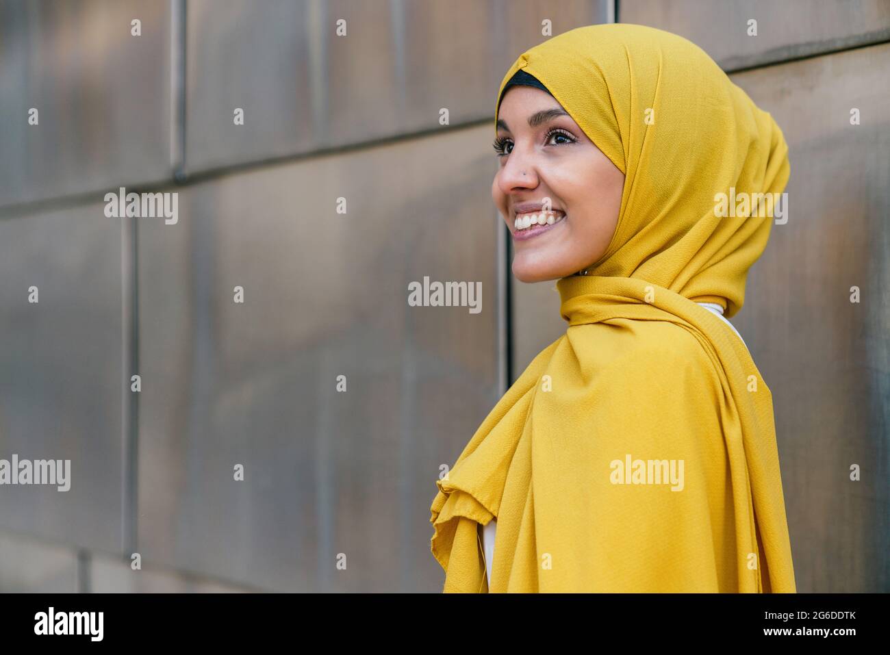 Side view of trendy Muslim female in yellow hijab standing in street ...