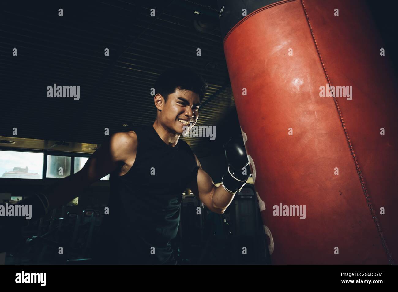 Young focused Asian man training boxing performing punches while ...