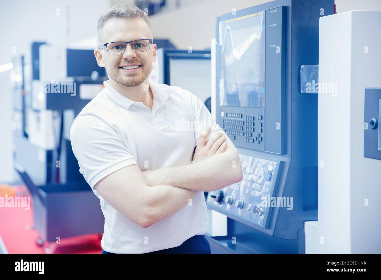 Engineer young man in glasses operates CNC automatic metalworking lathe ...